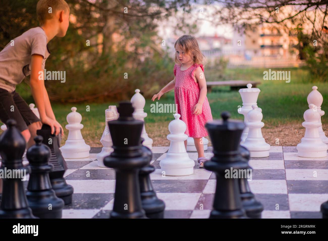Little Caucasian girl in a pink dress playing street chess. A child ...