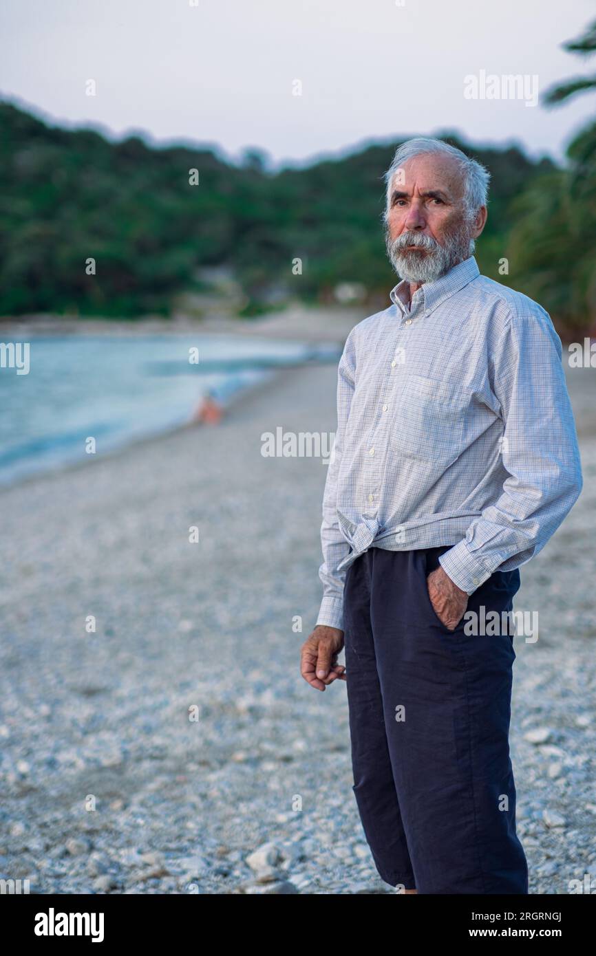 An old man on the beach in a white shirt and dark pants. An aged man ...