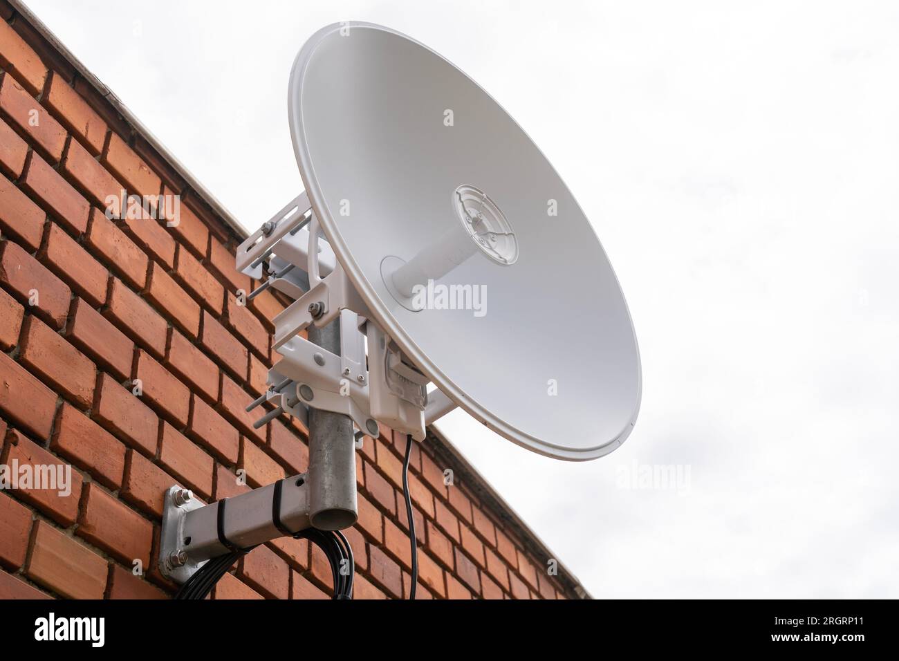 White satellite dish in front of brown brick wall Stock Photo - Alamy