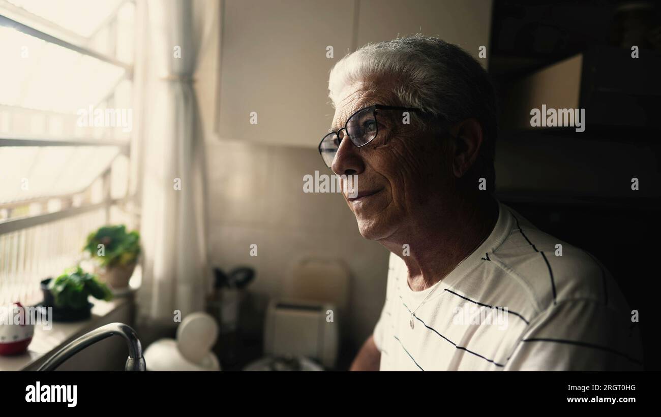 Contemplative older man staring out window in kitchen. Thoughtful ...