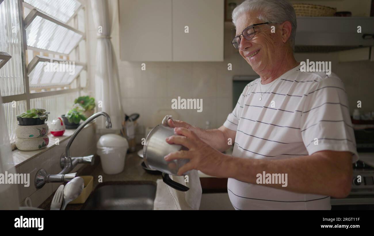 Happy senior man drying dishes by the kitchen sink. Authentic domestic ...