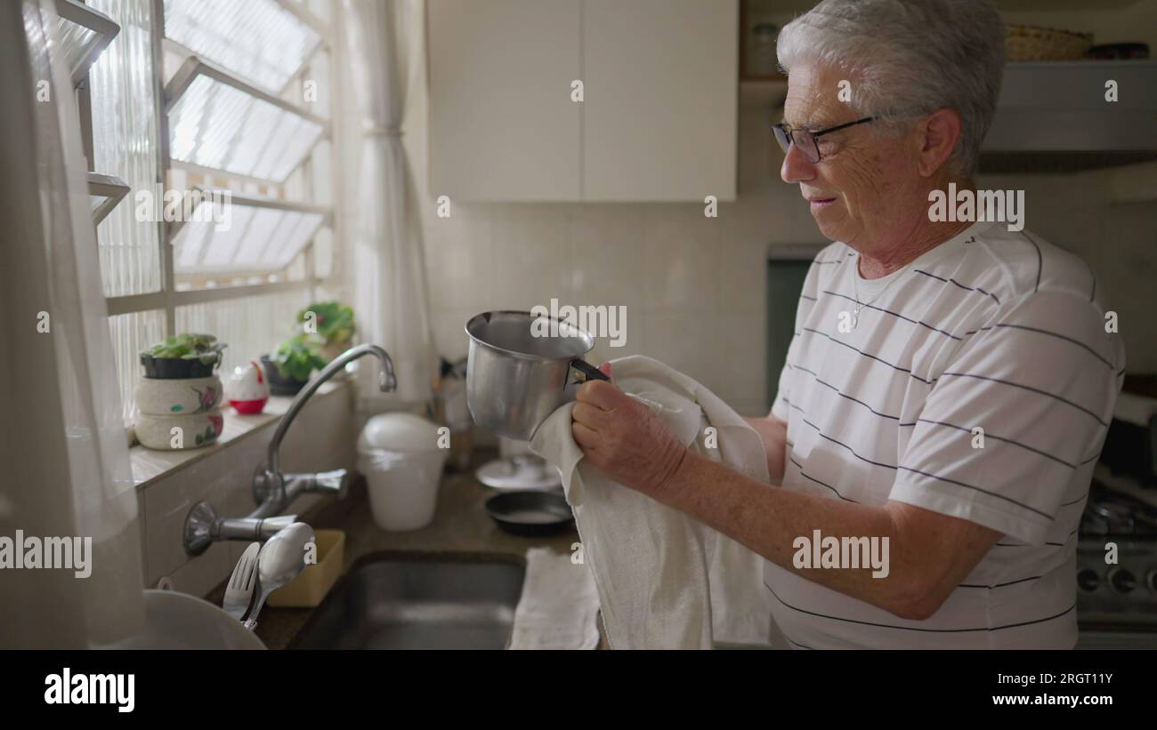 Happy senior man drying dishes by the kitchen sink. Authentic domestic ...