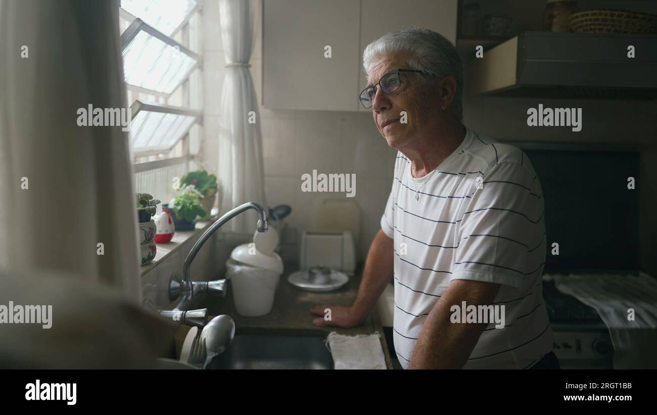 Thoughtful Senior Man Gazing Out of Kitchen Window, Leaning on Counter ...