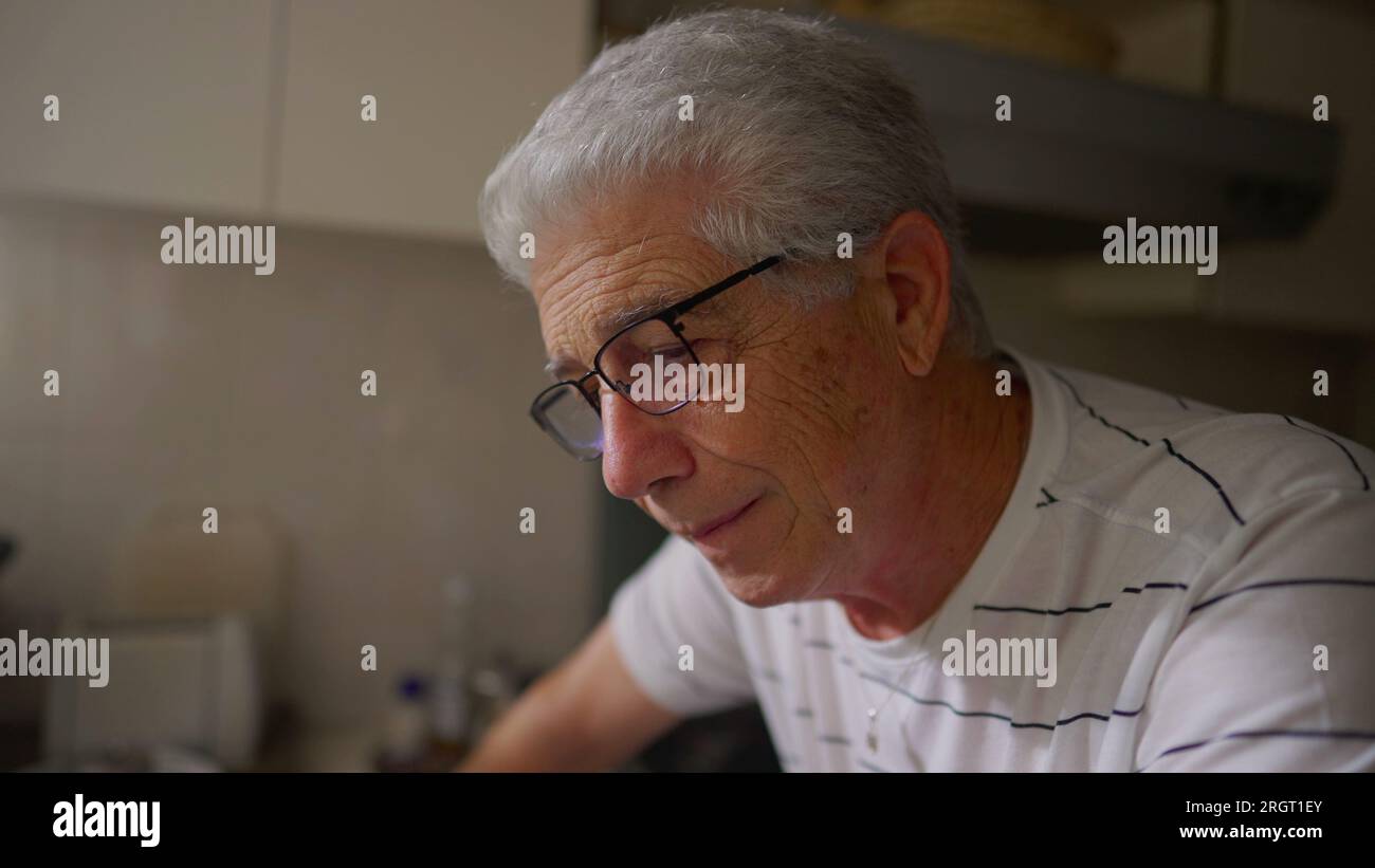 Worried senior man standing at kitchen counter leaning down by window ...