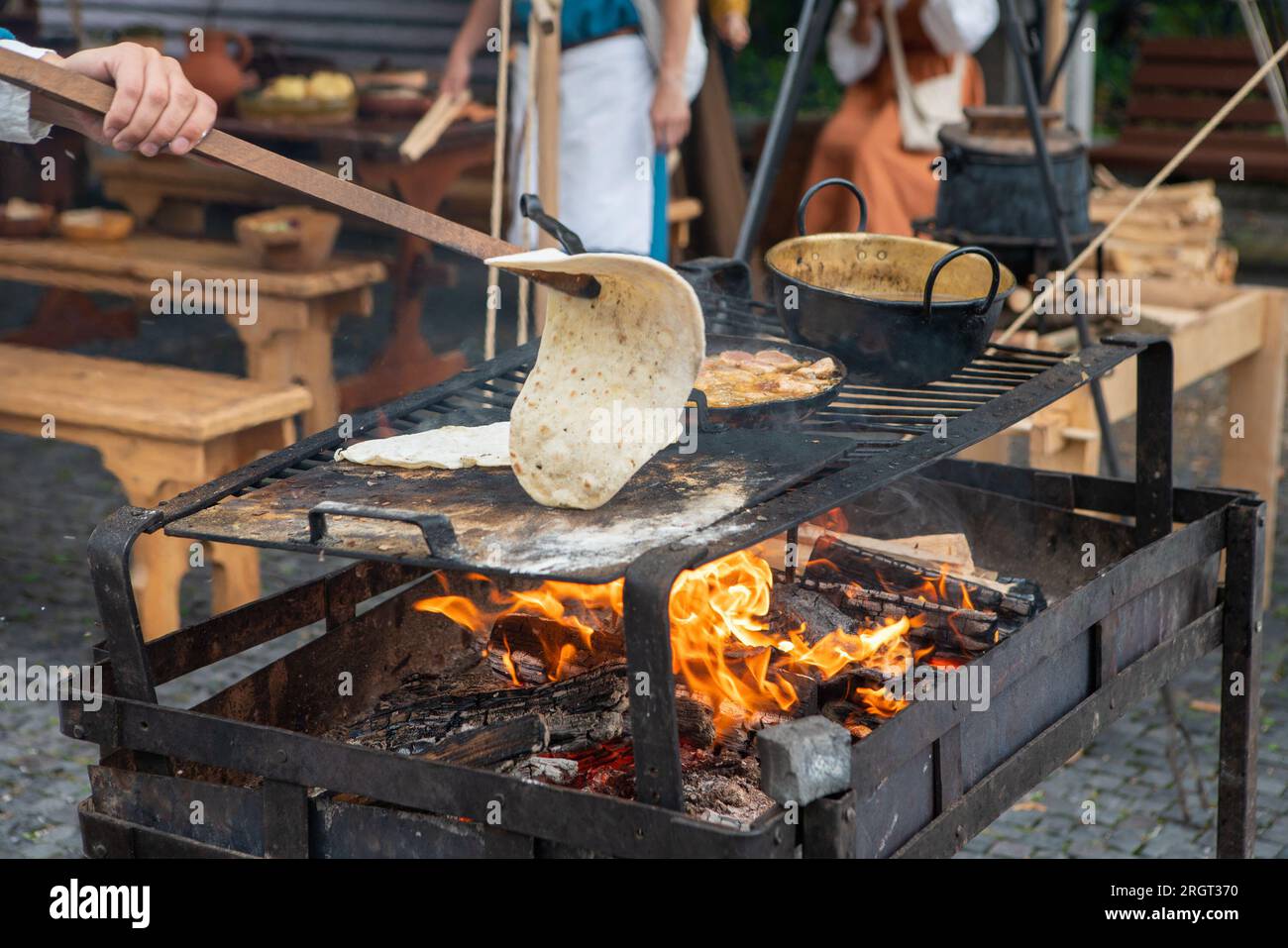 Woman preparing a natural flatbread on the open fire on the metal leaf ...