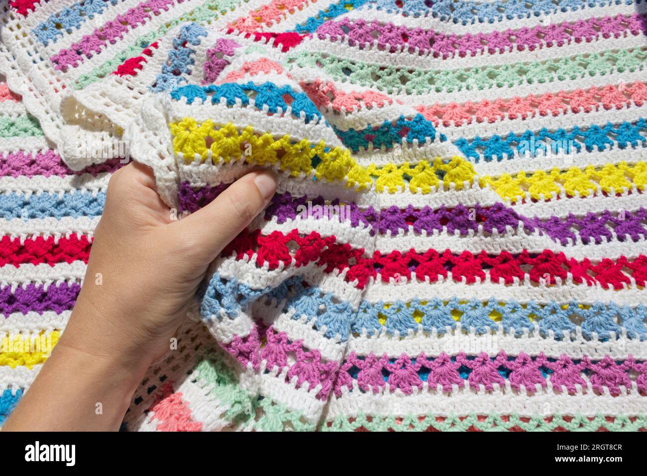 A hand touching a soft colored knitted blanket in the bright light of ...