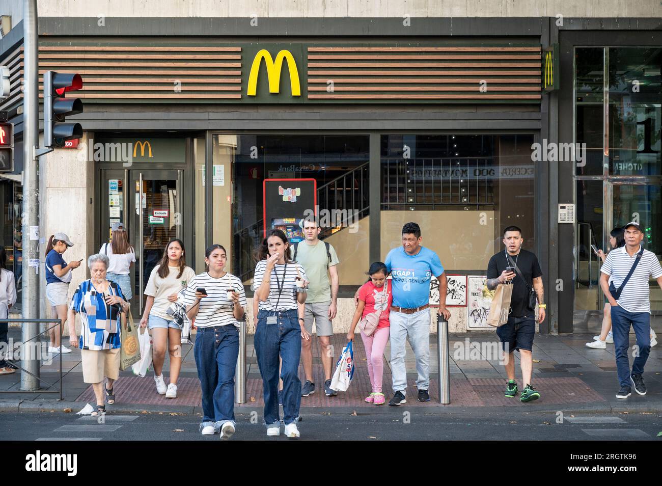 Pedestrians wait at a traffic light in front of an American ...
