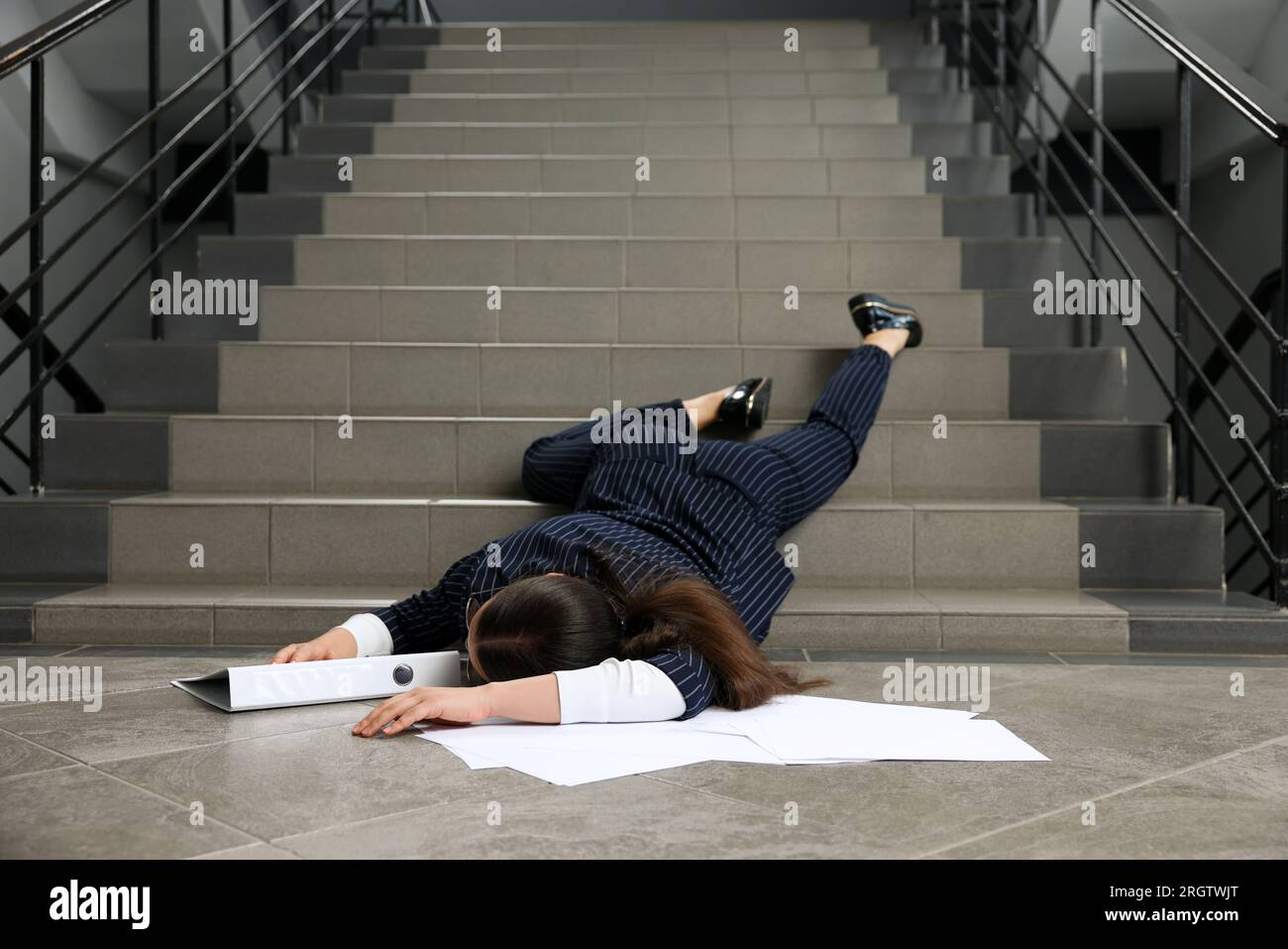 Unconscious woman with scattered folder and papers lying on floor after falling down stairs ...
