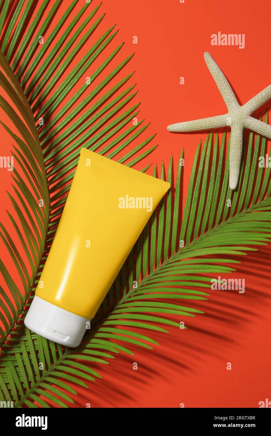 Sunscreen, starfish and tropical leaves on coral background, flat lay ...