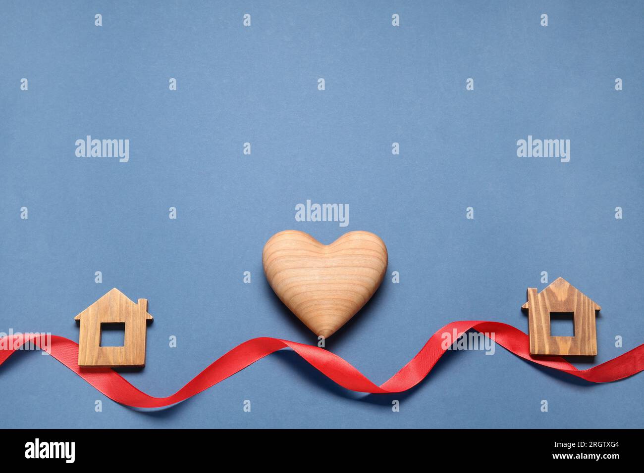 Decorative heart and red ribbon between two wooden house models on blue ...