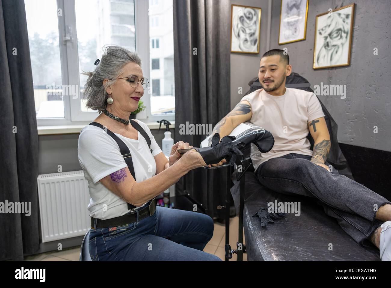 Mature female tattoo master working with the customer Stock Photo - Alamy