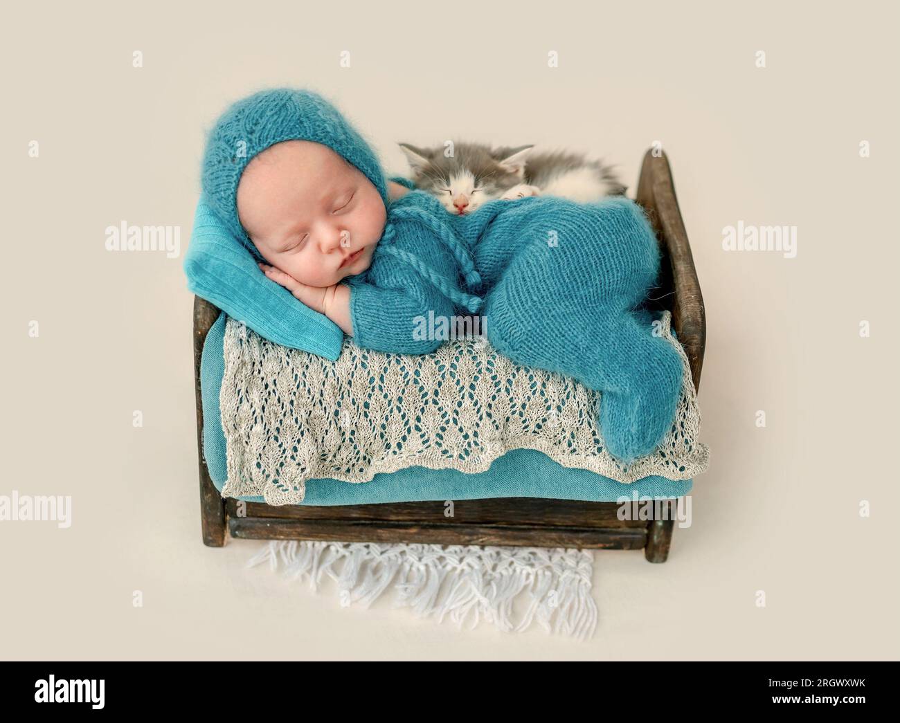 Newborn baby boy with kitty sleeping and holding hands under his cheeks ...