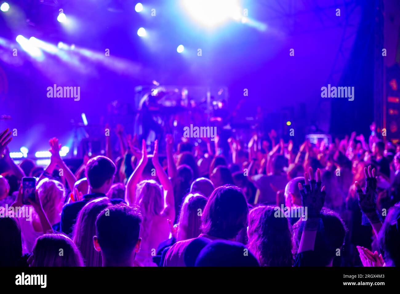 Back view of anonymous crowd with raised arms enjoying music show ...