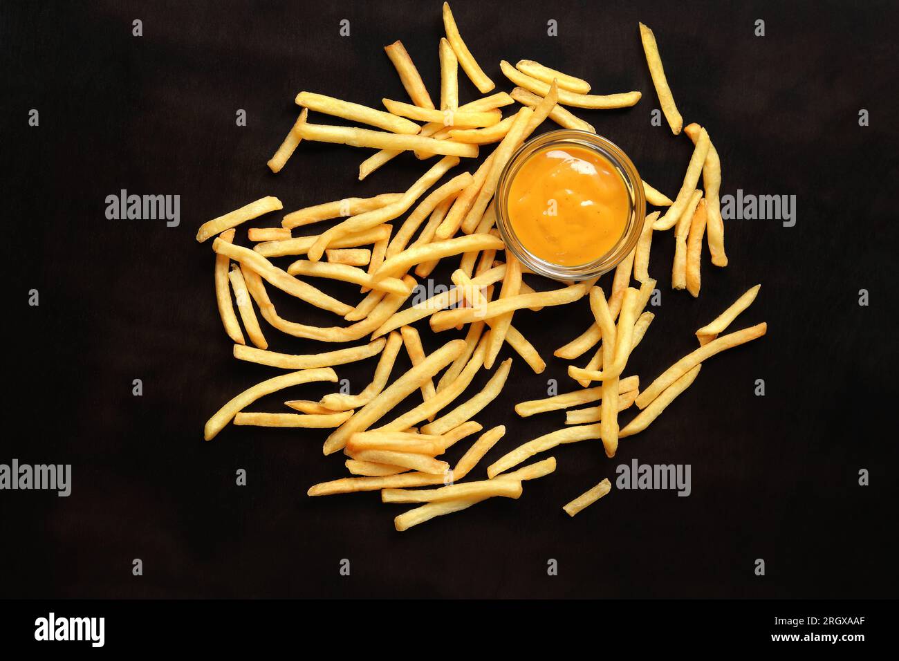 French fries scattered on a wooden dark table, mustard, top view. Fast ...
