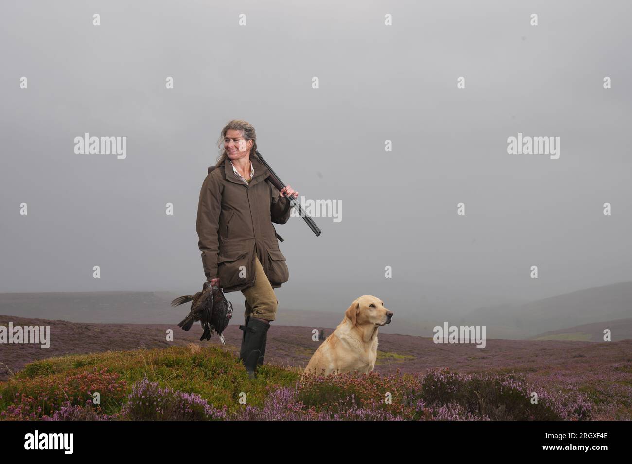 A woman carries grouse and a gun as she walks with her dog at a ...