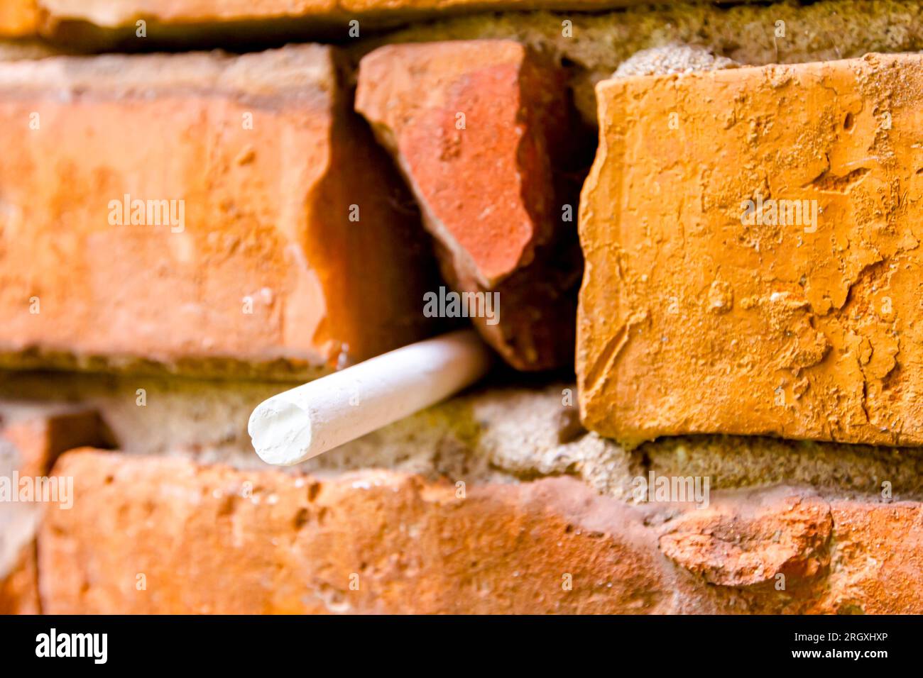 White school chalk stuck in an obsolete dilapidated wall of damaged red ...