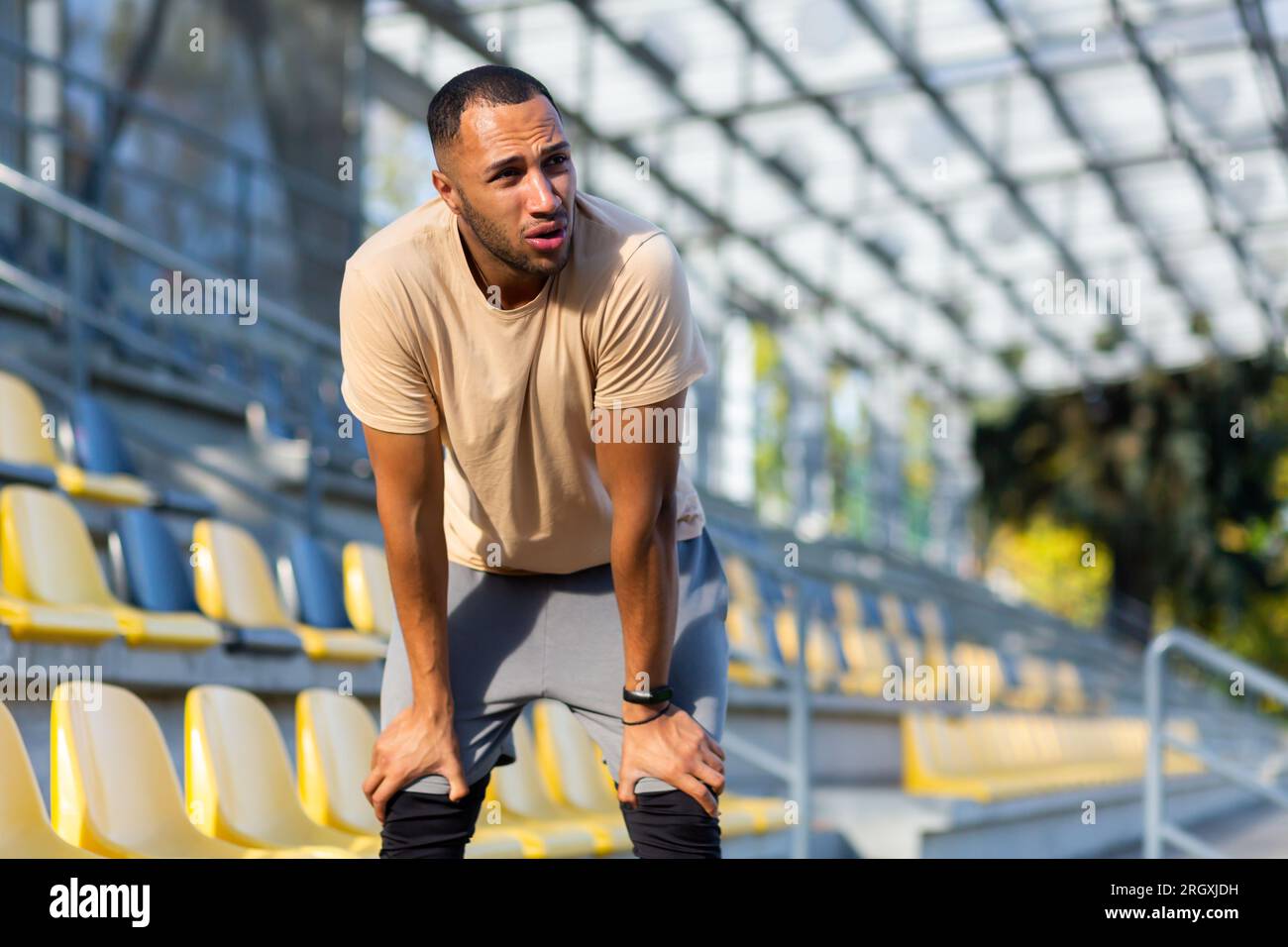 Tired hispanic athlete bent over and breathing after jogging, man doing ...