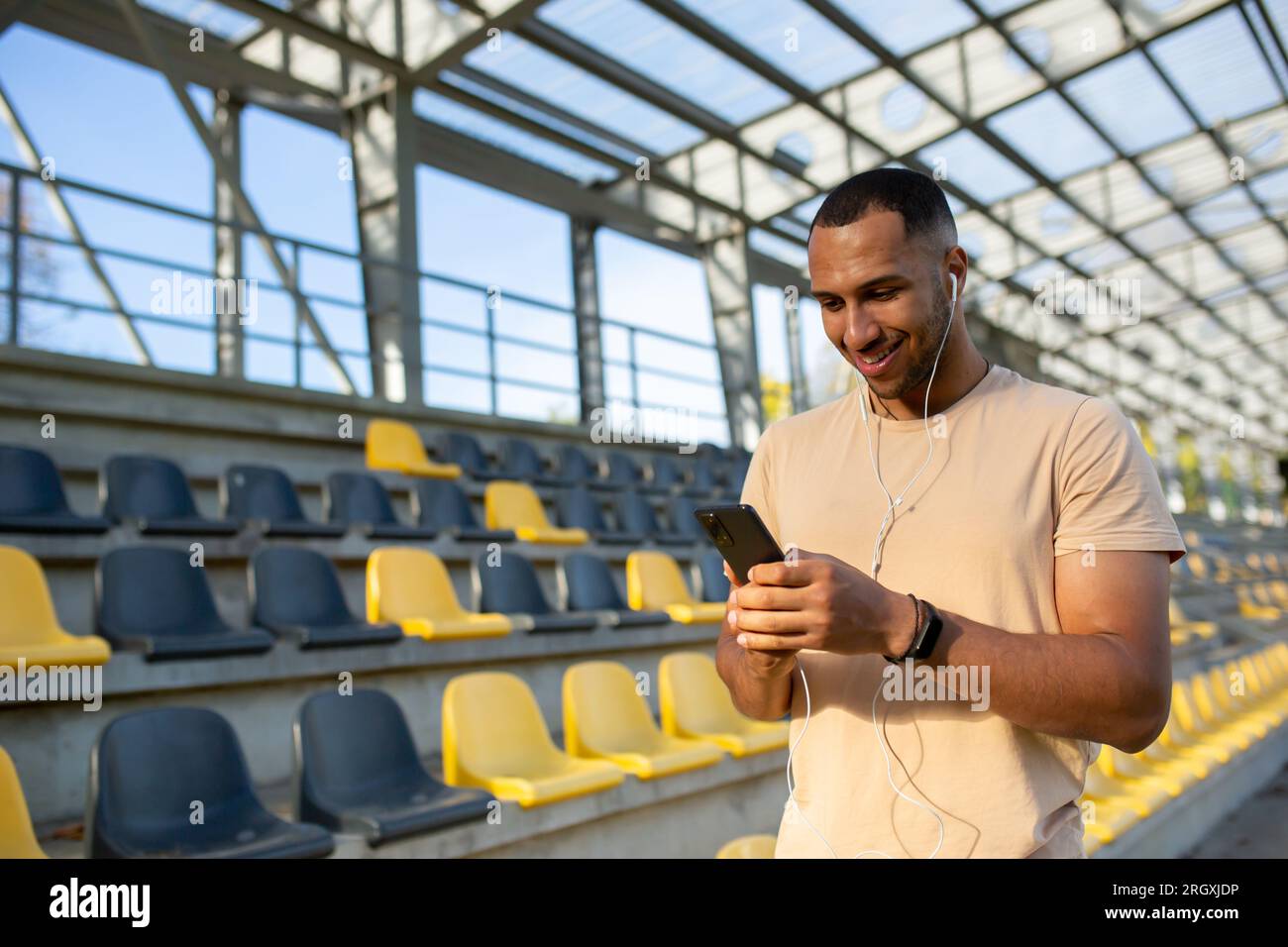 Male athlete uses app on phone after fitness class at stadium, trainer ...