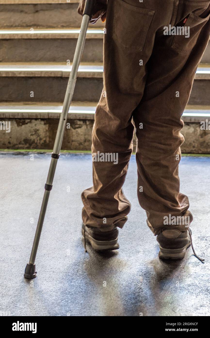 Disabled man's legs and feet with supporting cane in front of steps ...