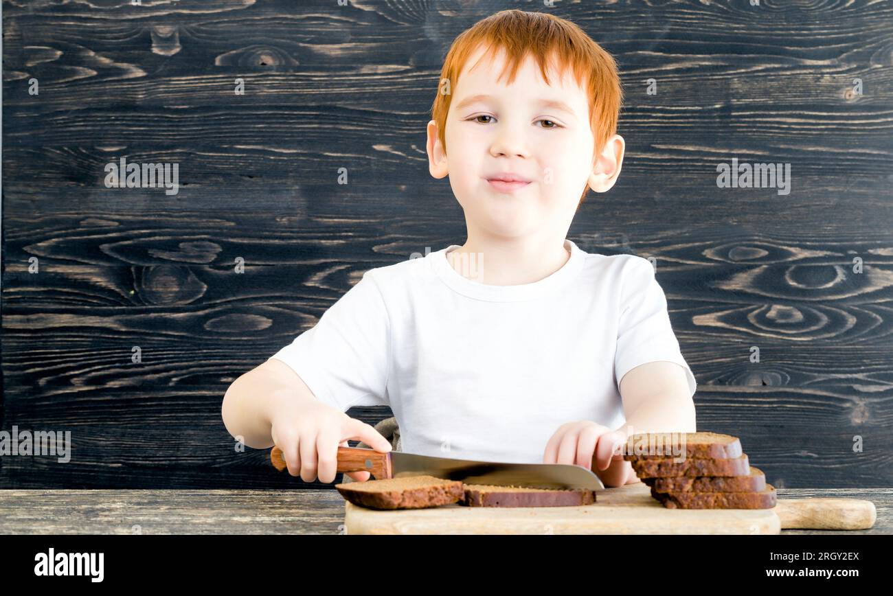 red-haired boy with a loaf of bread and a knife, closeup of working in ...