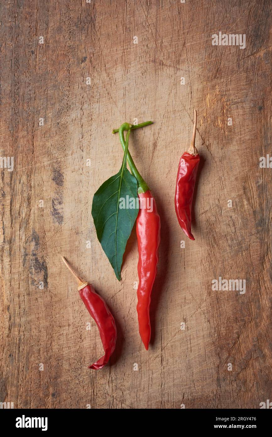 red chili, aka chili peppers or hot peppers with leaves on wooden table ...