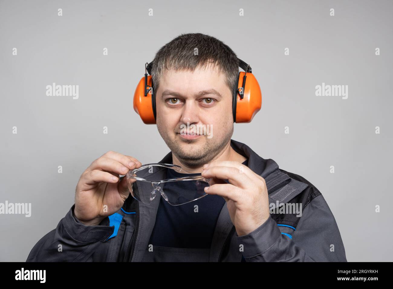 A builder wearing ear protectors wears goggles on a white background ...