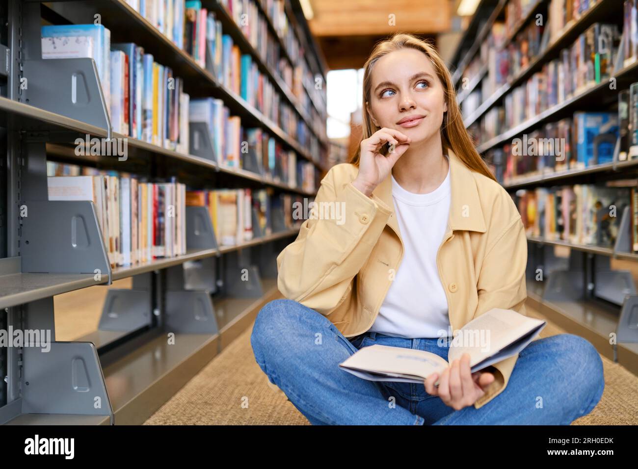 Smart girl student holding book sitting in university library on floor ...