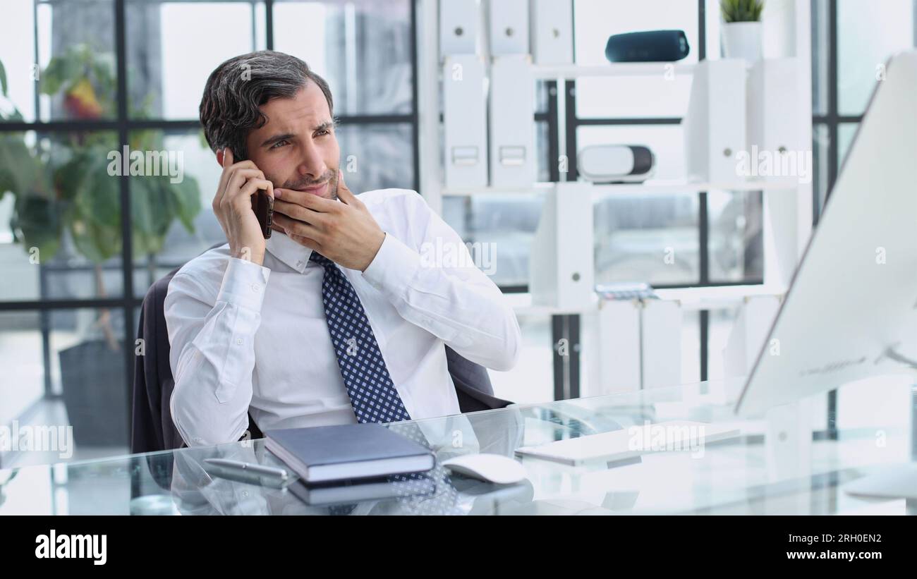 young web developer talking on phone while working with laptop in ...
