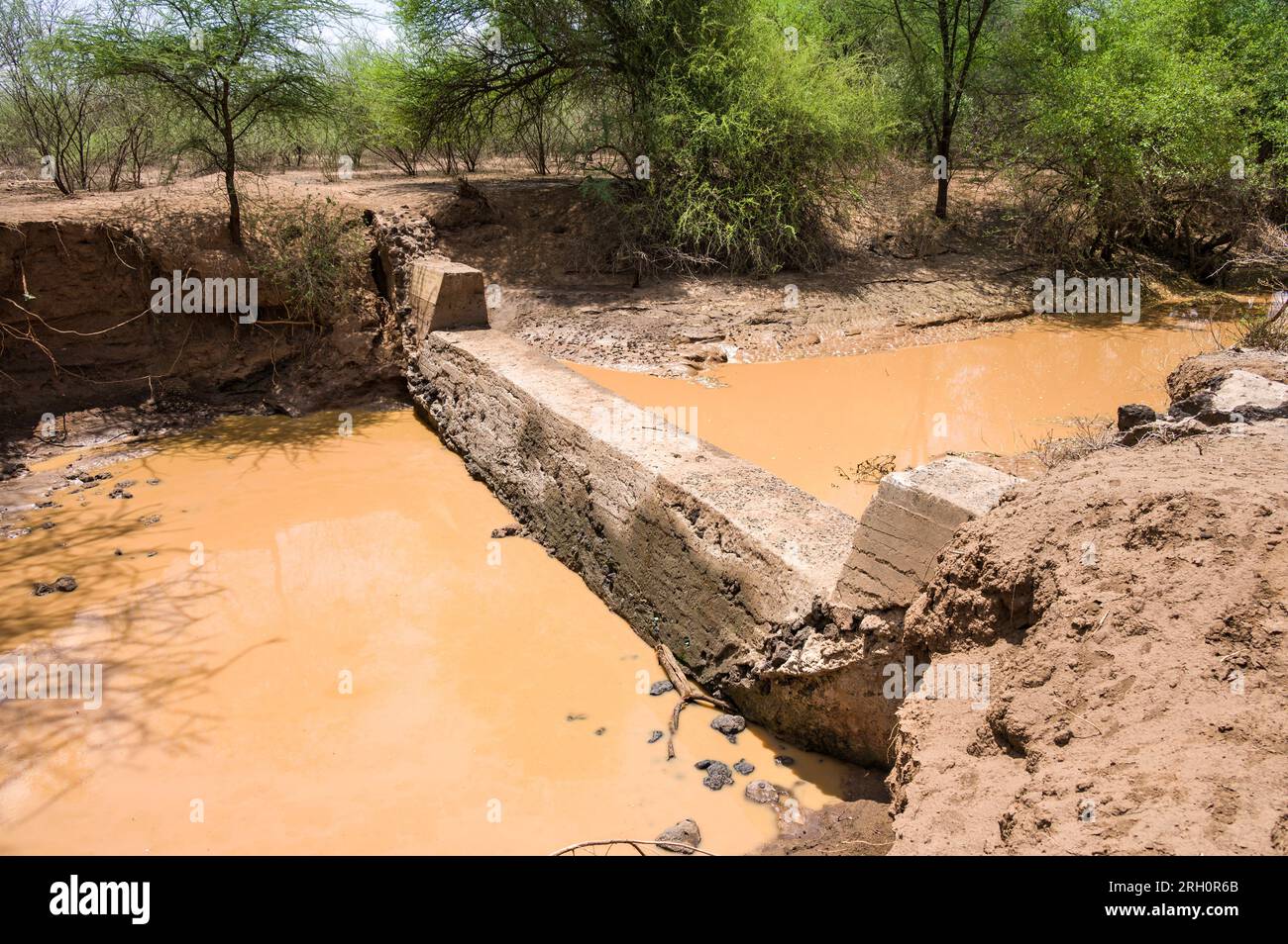 A concrete sand dam spanning a seasonal river with water on either side ...