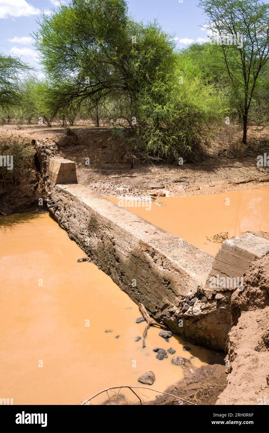 A concrete sand dam spanning a seasonal river with water on either side ...