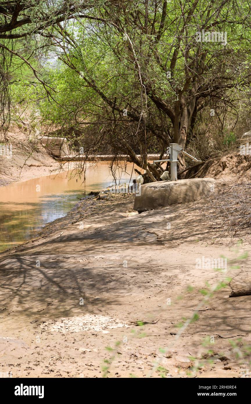A water hand pump upstream of a concrete sand bank with water stored ...
