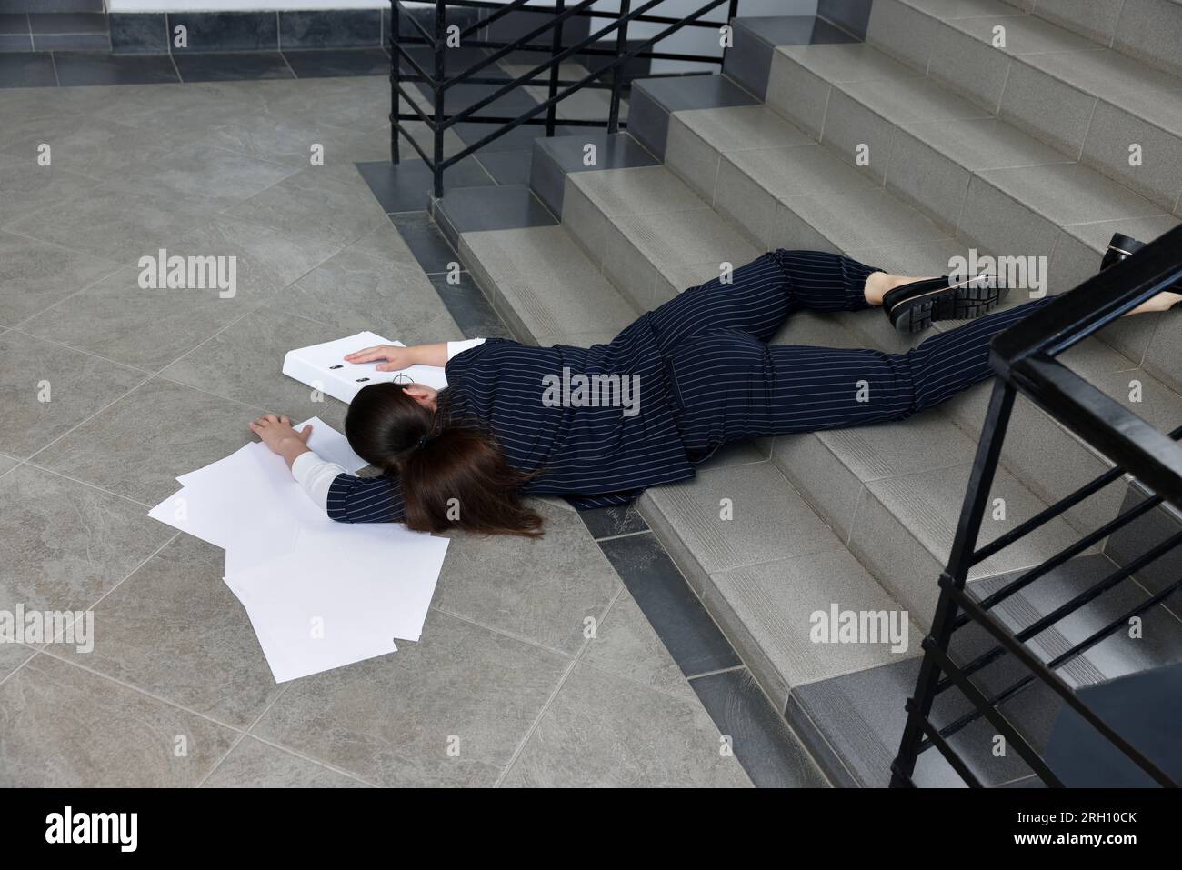 Unconscious woman with scattered folder and papers lying on floor after falling down stairs ...