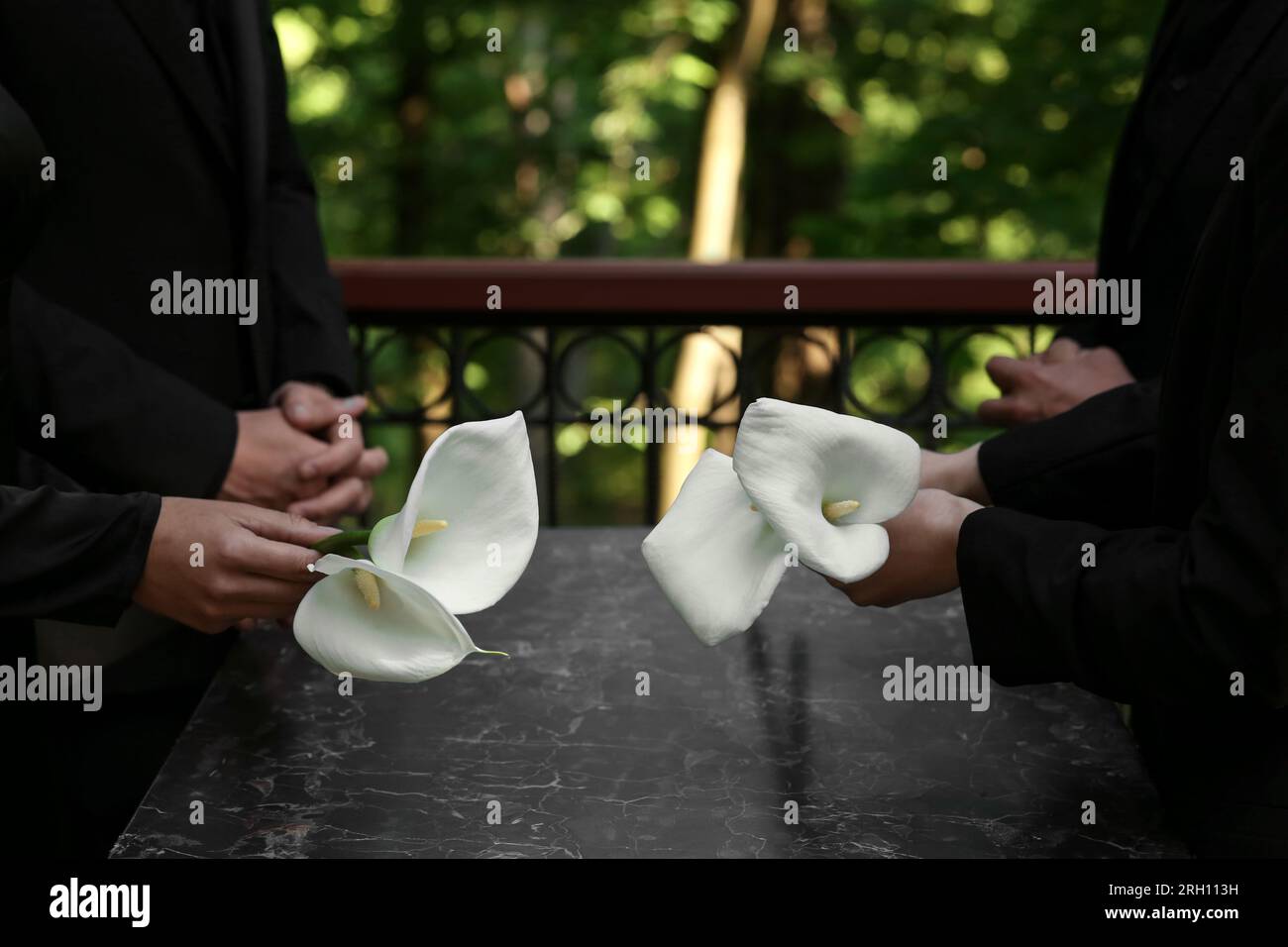 People with calla lily flowers near granite tombstone at cemetery ...