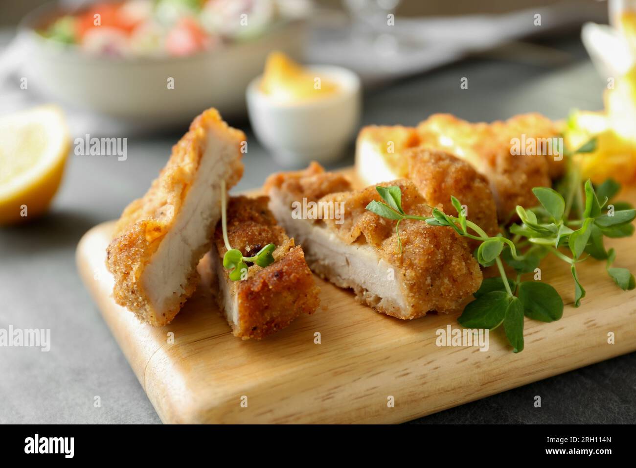 Delicious cut schnitzel served with microgreens on grey table, closeup ...