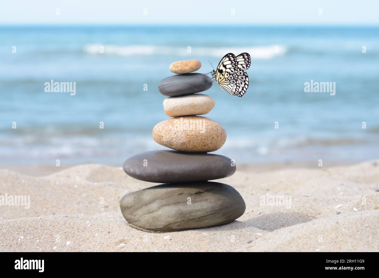 Peace and harmony. Stacked pebbles on sand and beautiful butterfly near ...