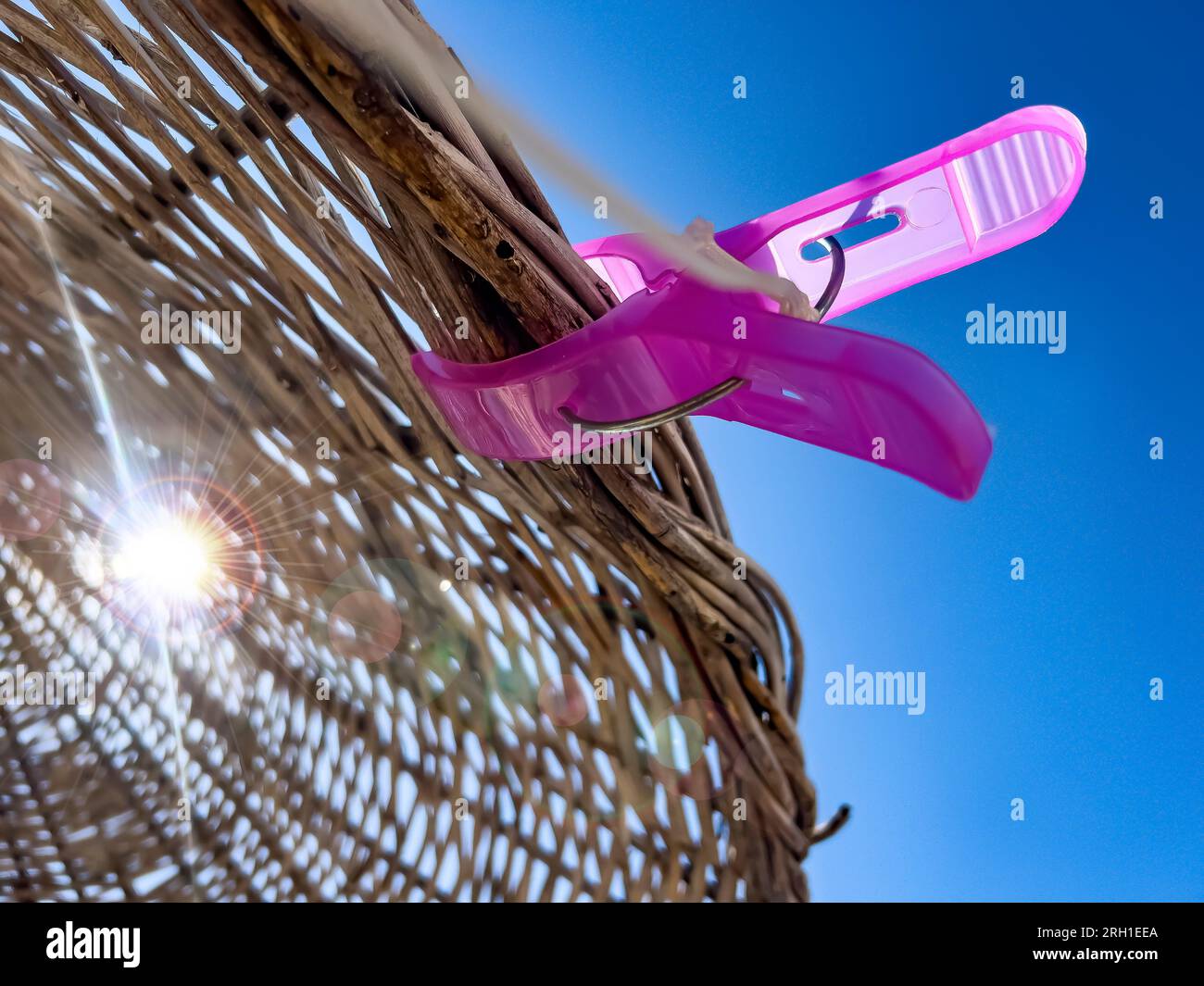Big pink clothes-pin at straw textured rattan parasol on the beach. Sun ...
