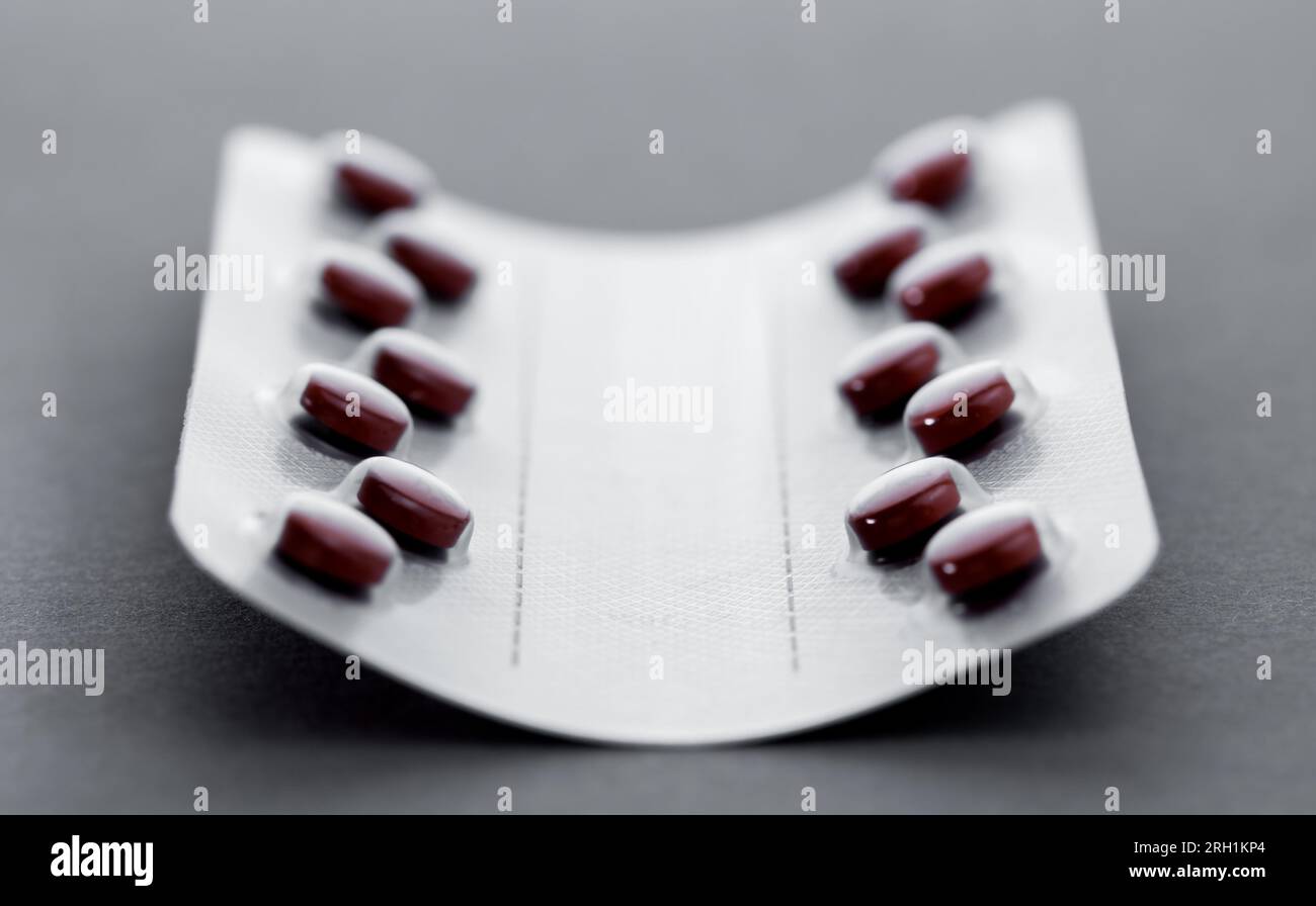 Foil packaging for tablets. Red pills in a blister pack lie on a dark ...