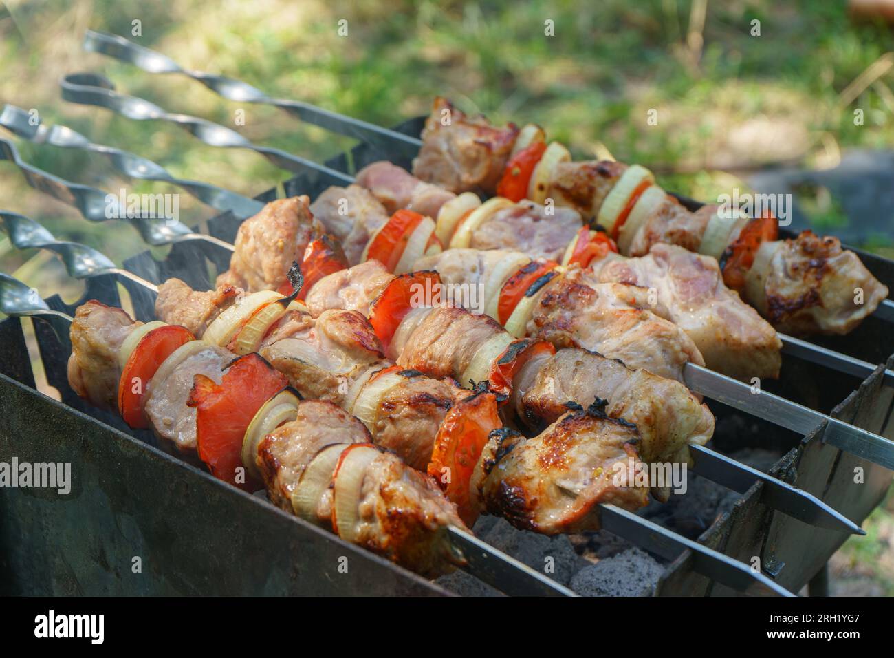 Grilled pieces of meat on skewers, shish kebab with vegetables, cooking process on fire, on ...