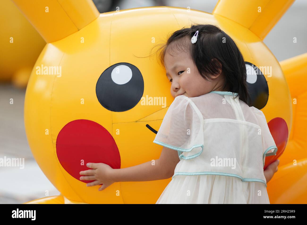 Yokohama, Japan. 13th Aug, 2023. A girl hugs an inflatable Pikachu at Minatomirai in Yokohama ...