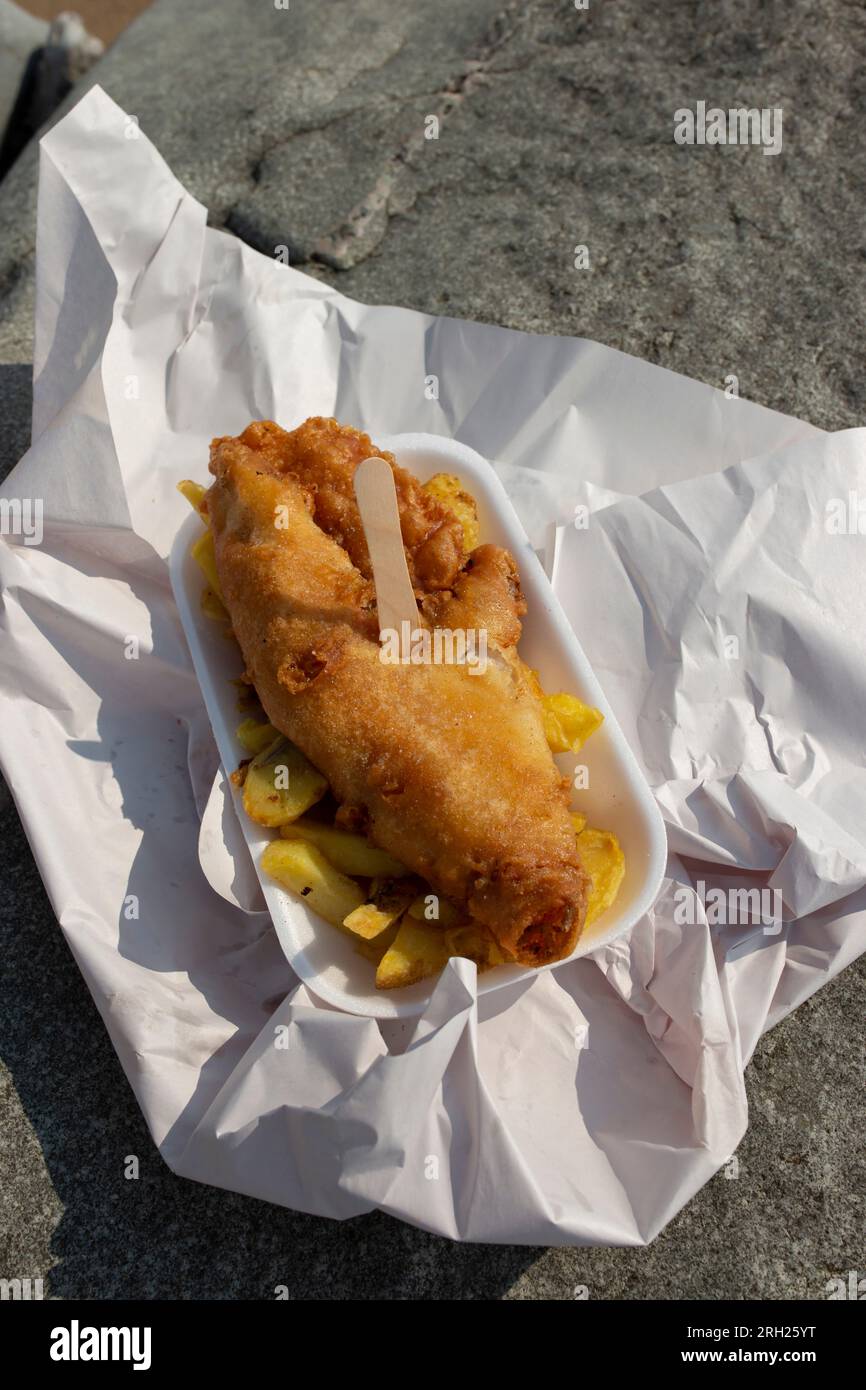 Fish and chips, battered cod, in a tray wrapped in paper with a wooden ...
