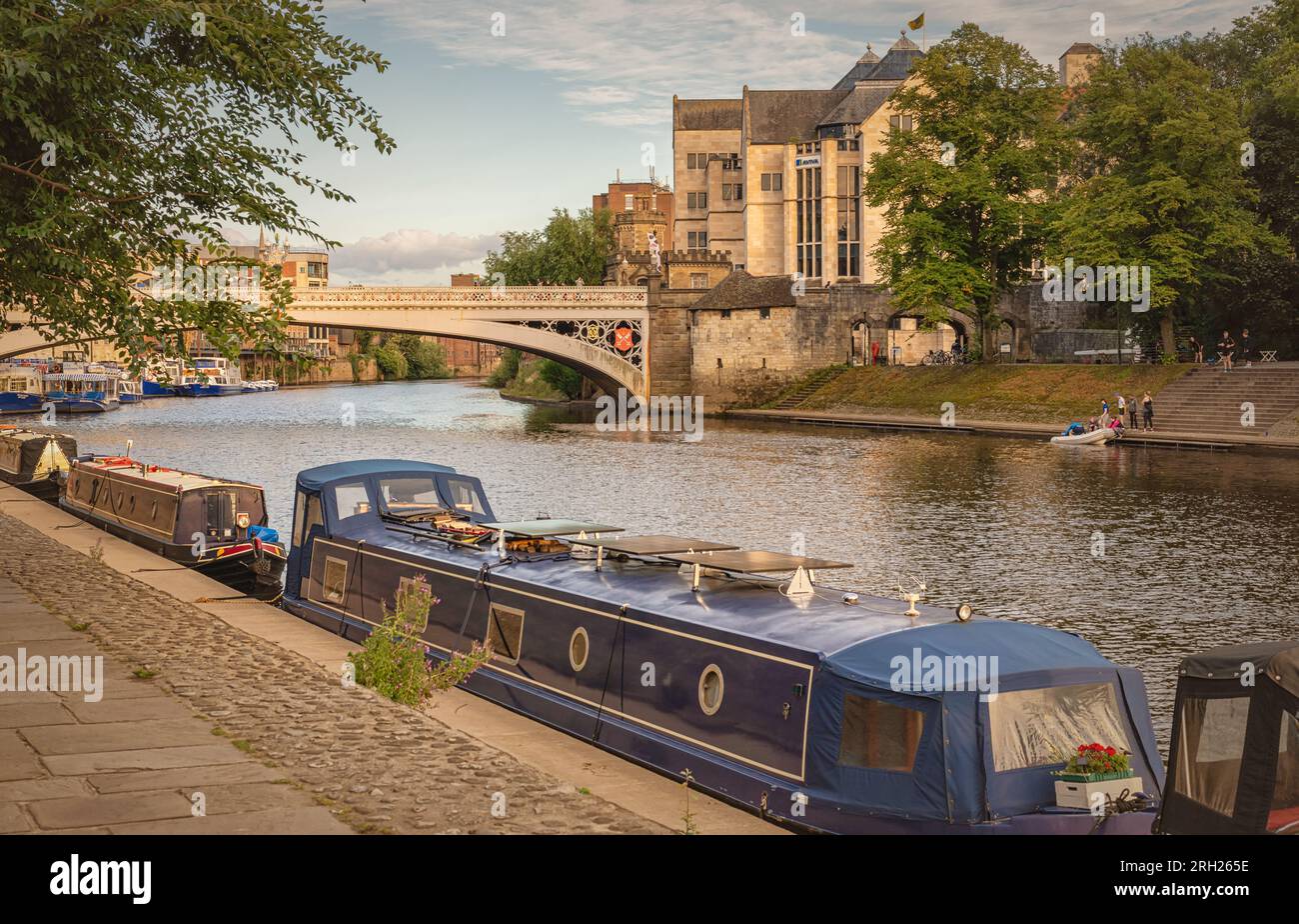 Canal boats line a riverbank and people recover a dinghy. A historical ...
