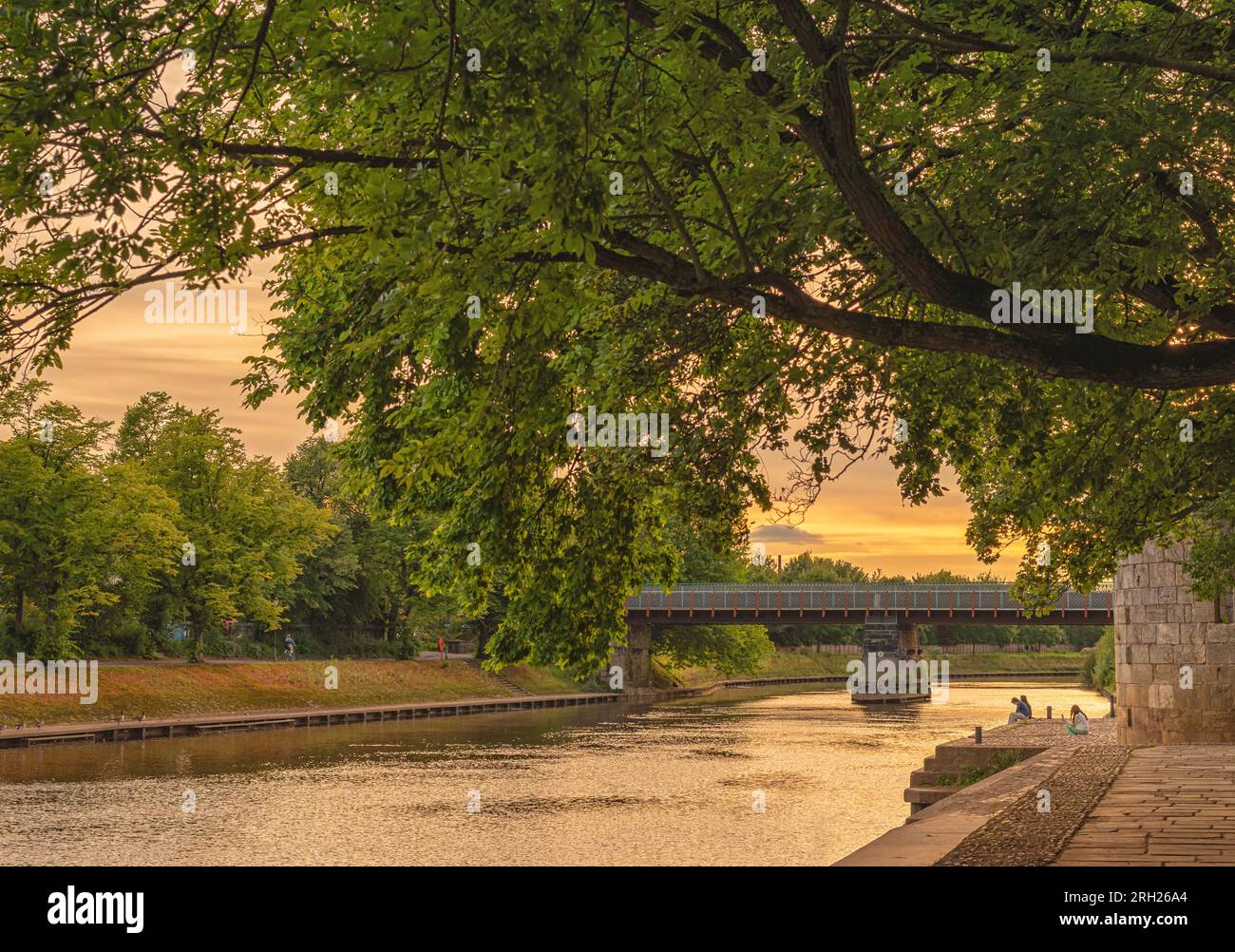 People are sat on a cobbled wharf at sunset. An ancient defence tower ...