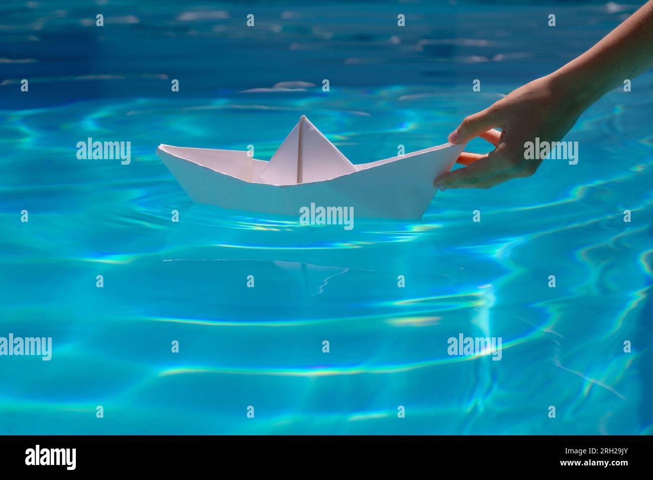 Paper boat sailing on water causing waves and ripples. Hand putting a ...