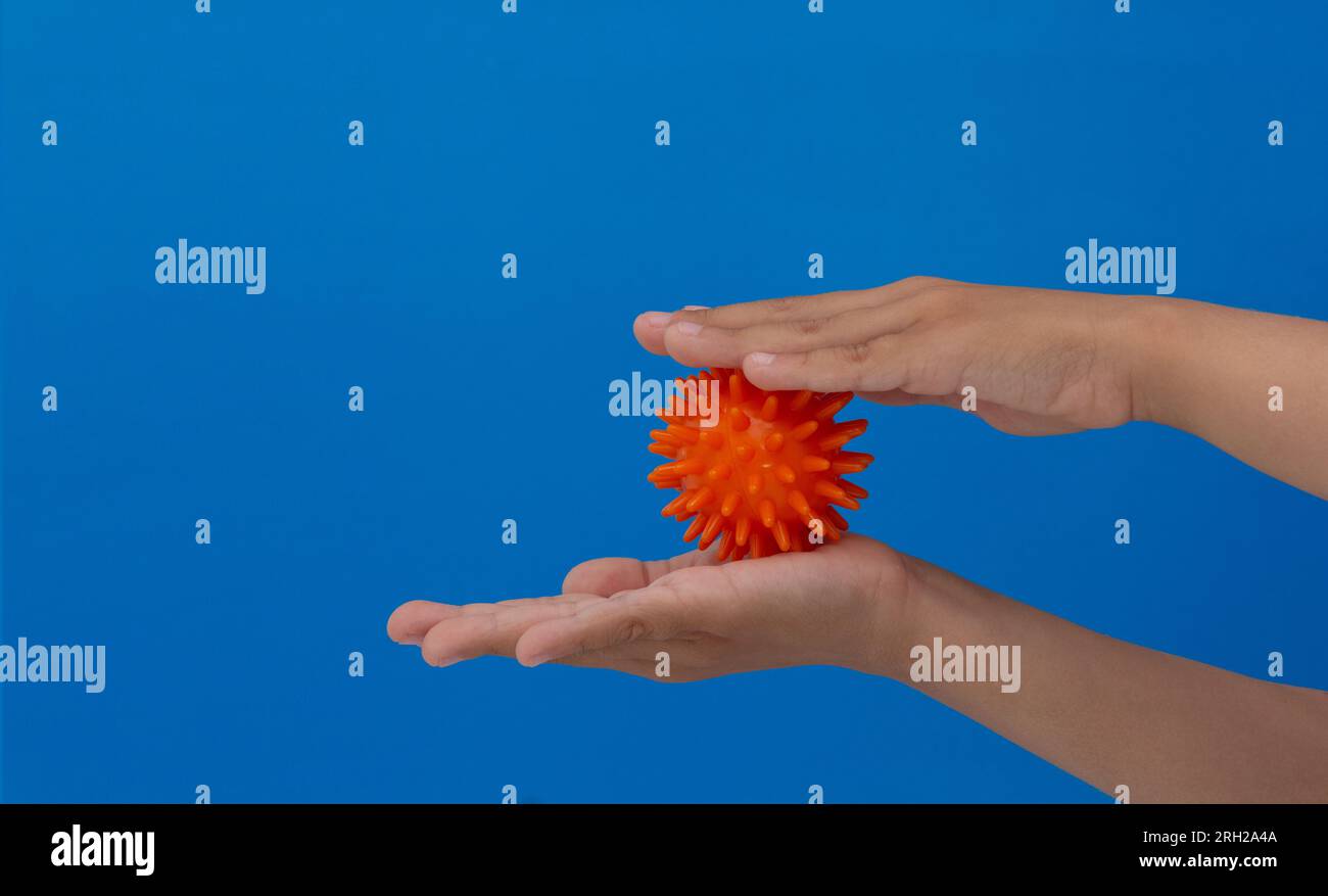 Child hands rolling spiky orange massage needle ball between palms over ...