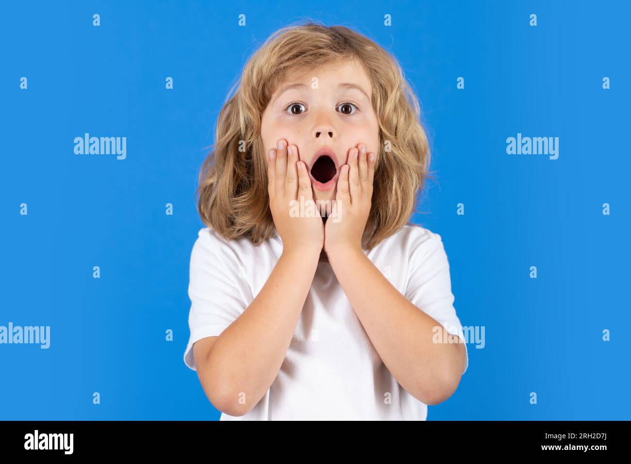 Shocked child boy keeping hands near cheek with open mouth on studio ...