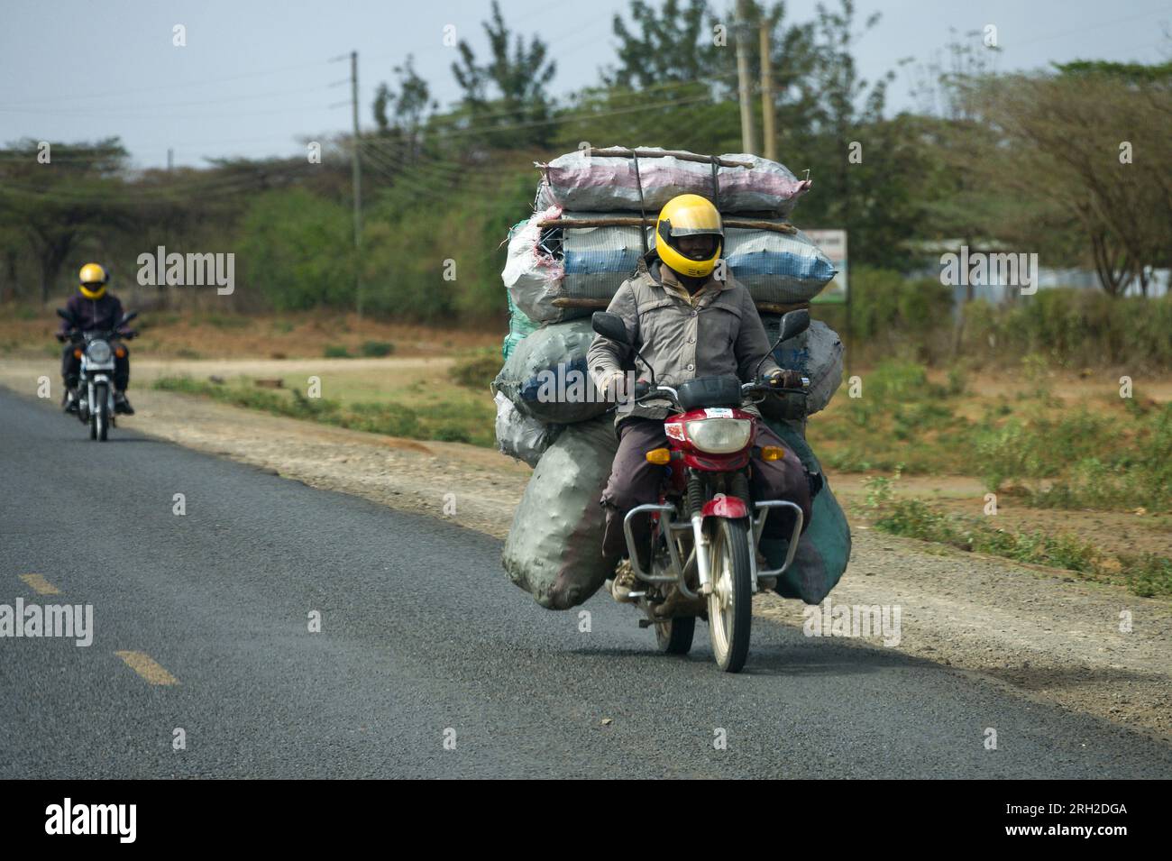 A male boda boda motorbike rider carrying sacks of charcoal on the back ...