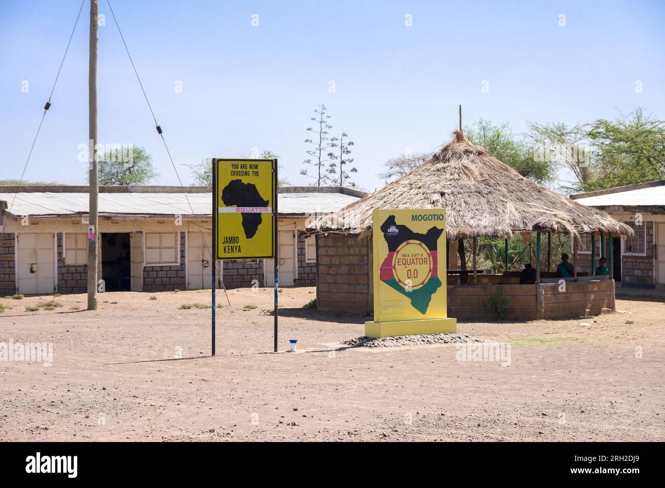 A sign stating you are crossing the equator with buildings behind it ...