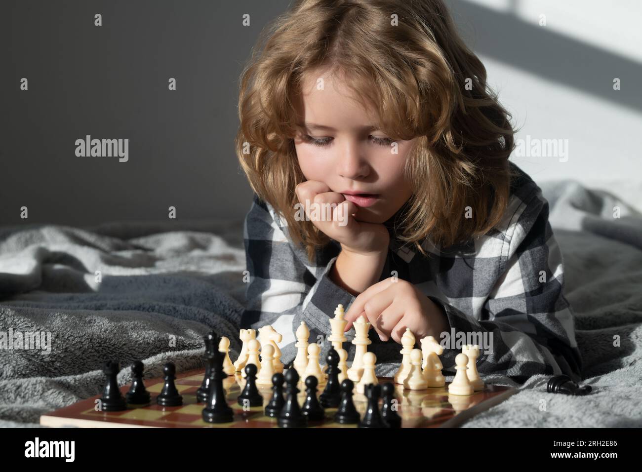 Child playing chess on bed. Clever child thinking about chess. Portrait ...