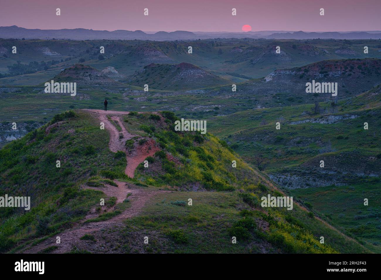 Woman standing on hilltop watches sunrise through haze over the ...
