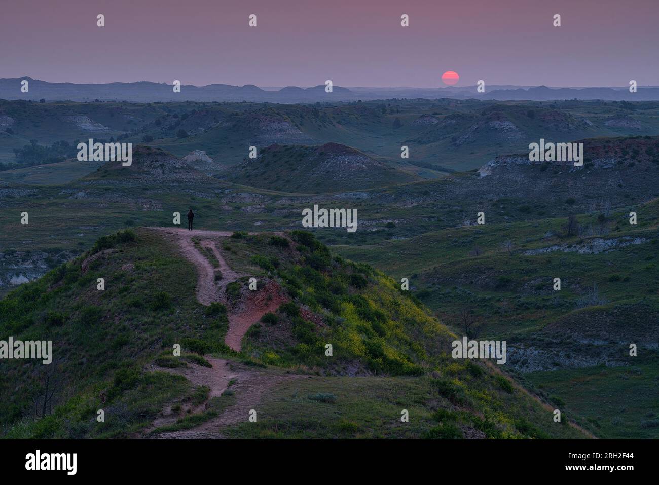 Woman standing on hilltop watches sunrise through haze over the ...